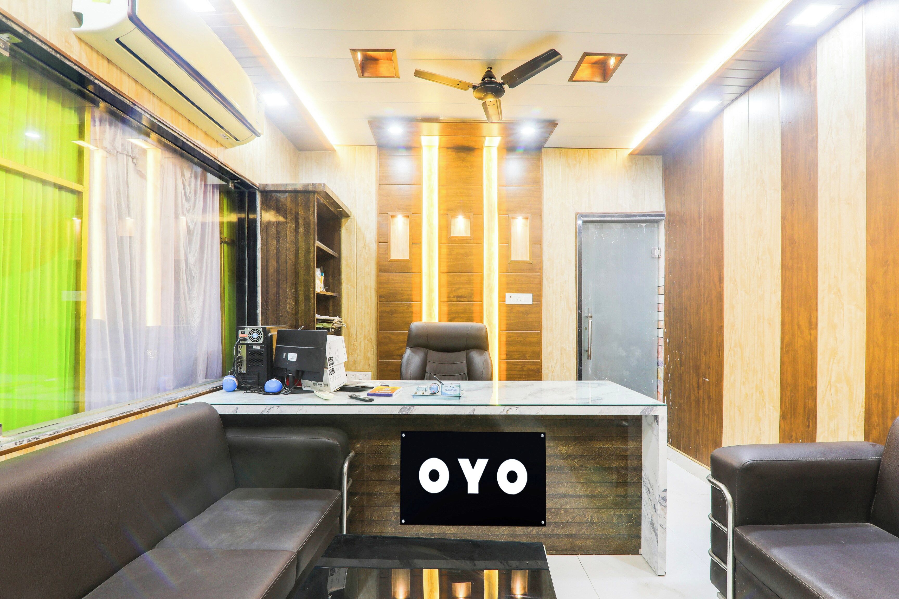 Balcão de recepção com placa indicando 'OYO', um ventilador de teto e uma janela com cortinas.
