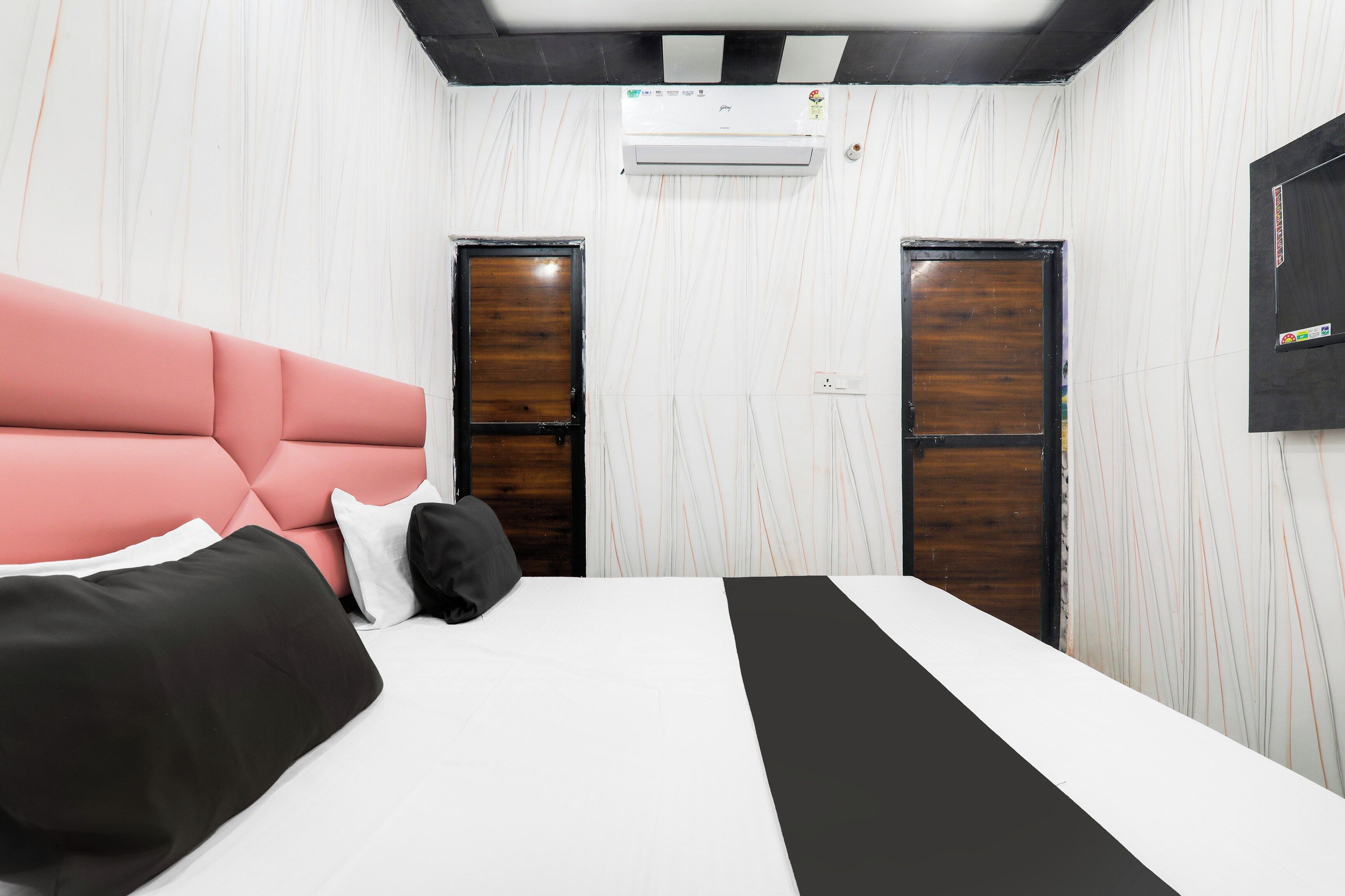Quarto com cama, cabeceira rosa, duas portas e aparelho de ar condicionado.