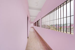 Um corredor com paredes cor-de-rosa, piso ladrilhado e grandes janelas com grades de metal.
