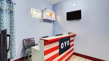 Uma receção com uma placa a dizer 'OYO' num hall de hotel com paredes azul claro, cortina estampada e uma televisão de ecrã plano montada na parede.