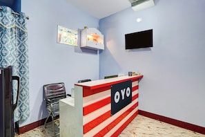 Uma receção com uma placa a dizer 'OYO' num hall de hotel com paredes azul claro, cortina estampada e uma televisão de ecrã plano montada na parede.