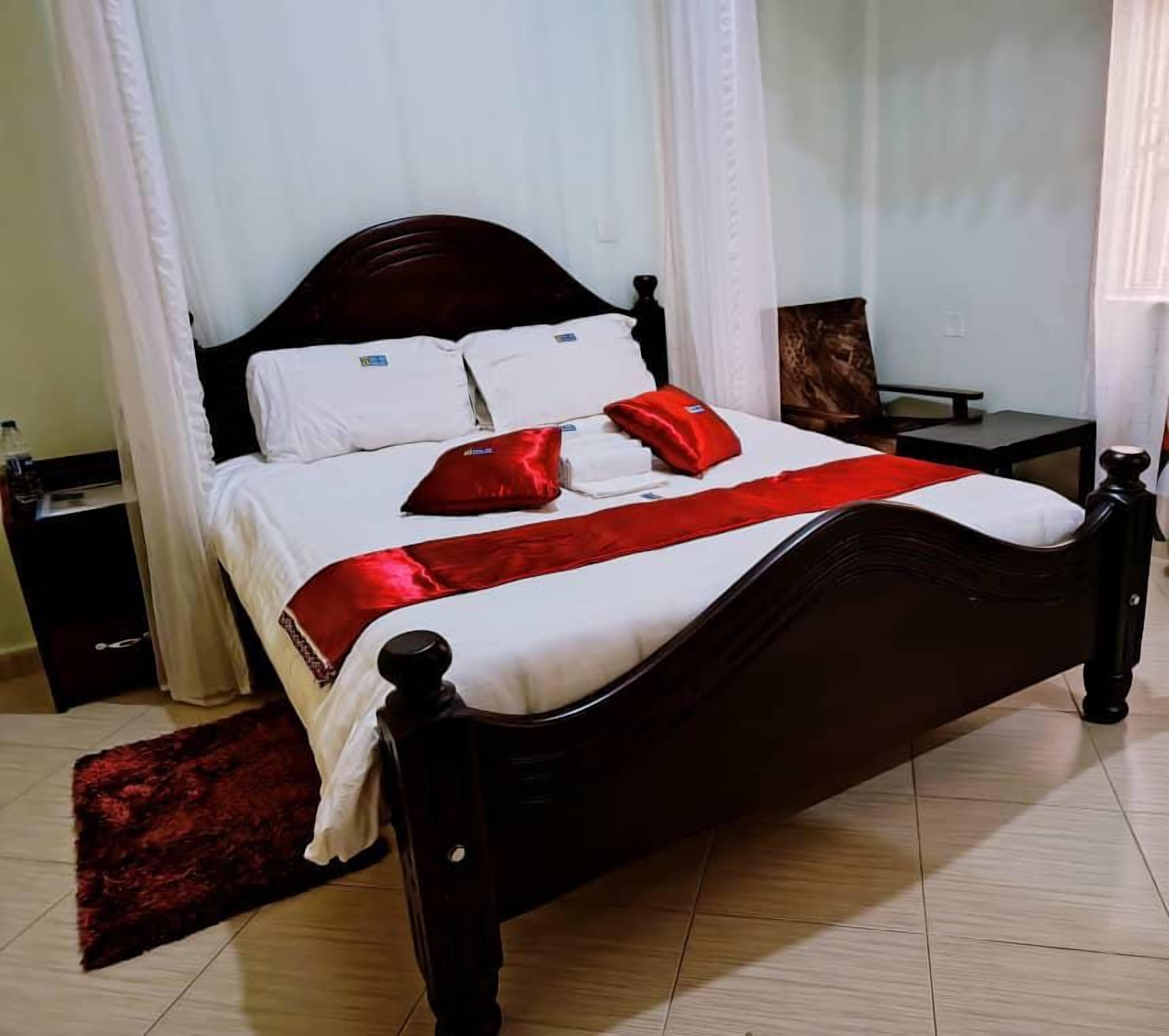 Cama com estrutura de madeira escura, roupa de cama branca e detalhes vermelhos.