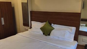 Quarto de hotel com uma cama grande, cabeceira de madeira, mesa de cabeceira e guarda-roupa.