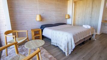 Quarto com cama, duas cadeiras, uma mesinha e chão de madeira.