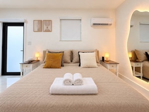Quarto de hotel com cama, duas mesas de cabeceira, ar condicionado fixado na parede, espelho e uma porta.