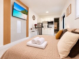Quarto de hotel com cama, TV na parede, área de cozinha e vista para a praia.