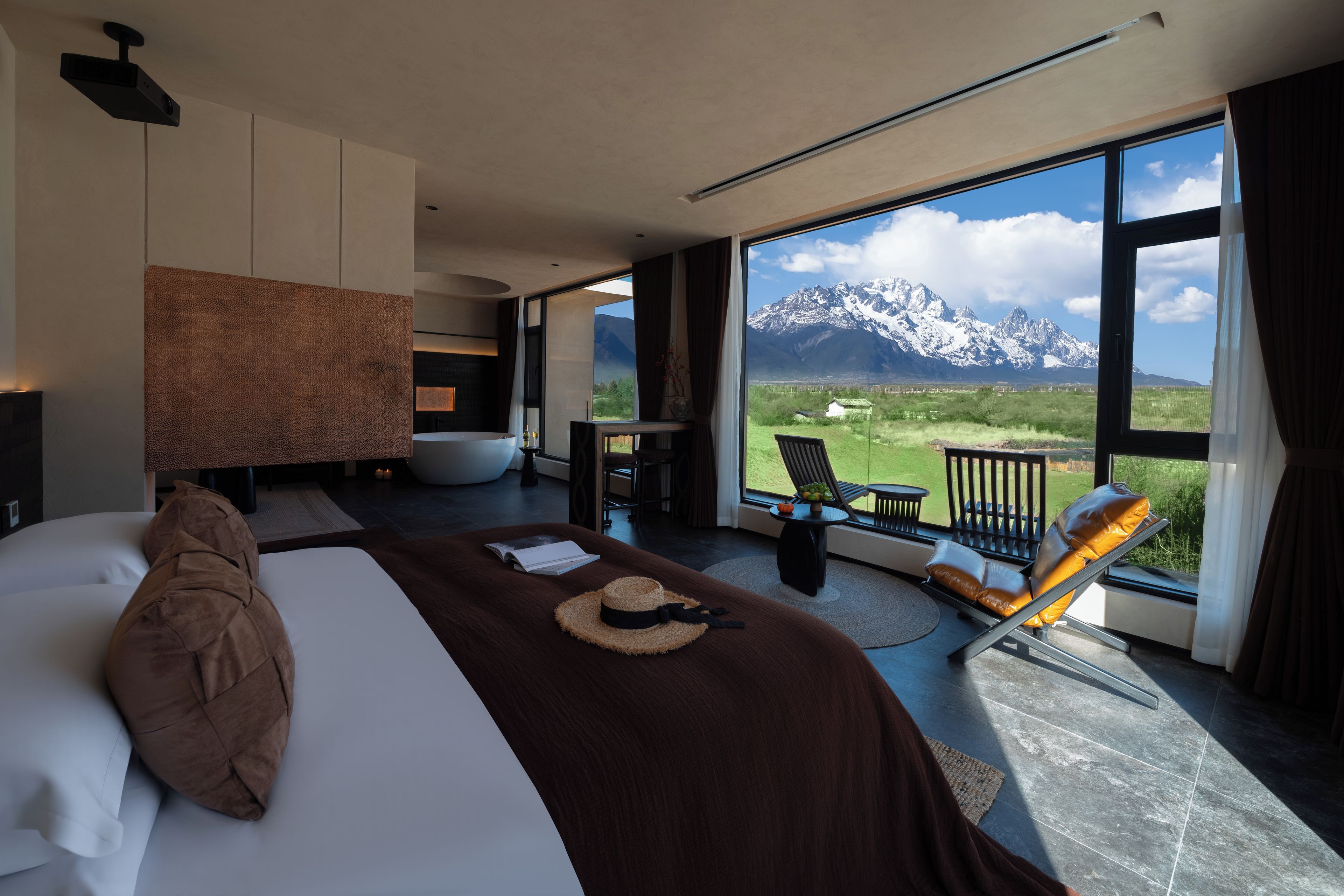 Quarto de hotel moderno com uma cama grande, vista para montanhas e varanda com uma cadeira.