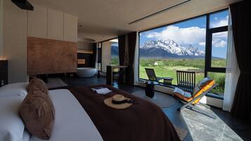 Quarto de hotel moderno com uma cama grande, vista para montanhas e varanda com uma cadeira.
