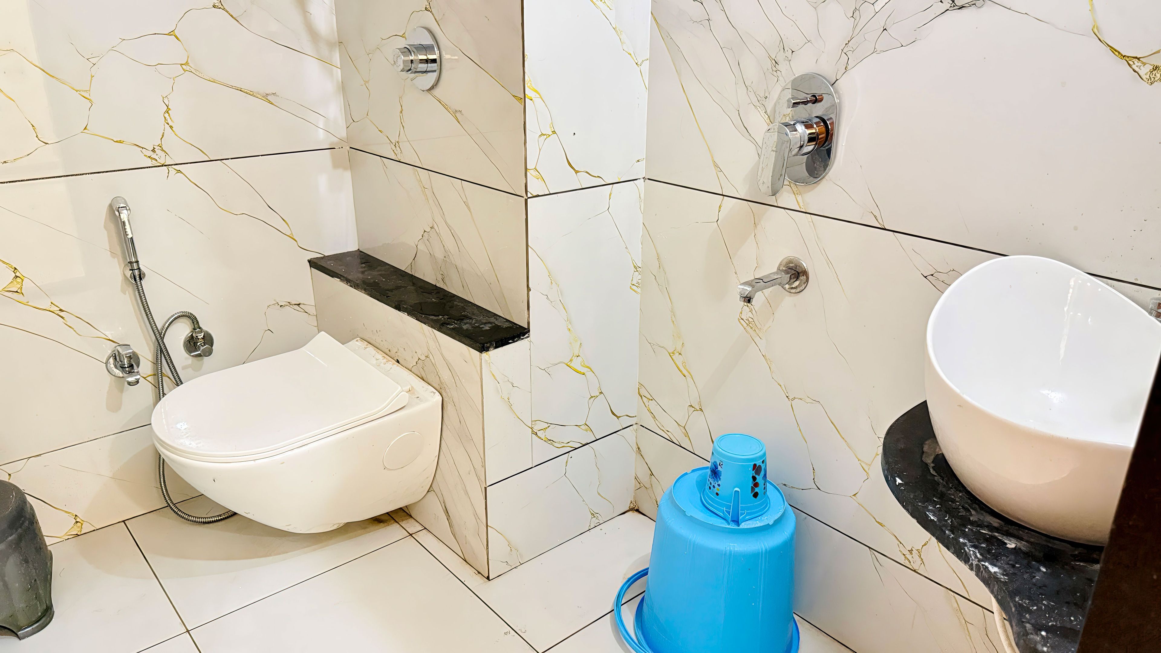 Casa de banho com sanita, lavatório, chuveiro e dispensador de água azul.