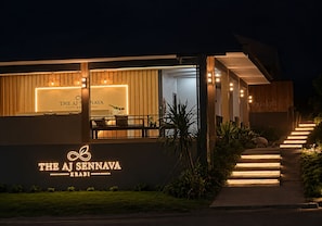 Um edifício moderno com uma placa indicando 'The AJ Sennava Krabi' à noite.