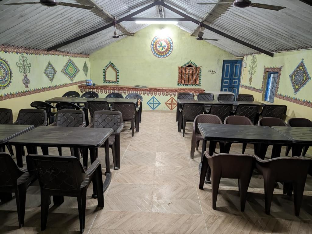 Quarto com teto alto, paredes padronizadas e um ventilador de teto central. Mesas e cadeiras dispostas para refeições.