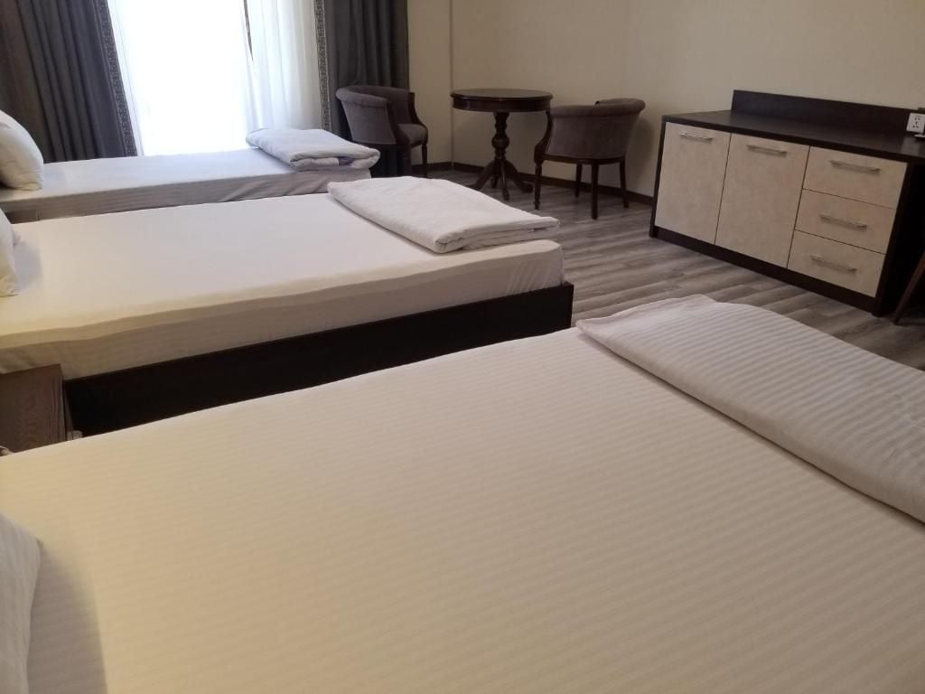 Quarto de hotel com duas camas, uma escrivaninha, uma cadeira, uma mesinha e um armário.