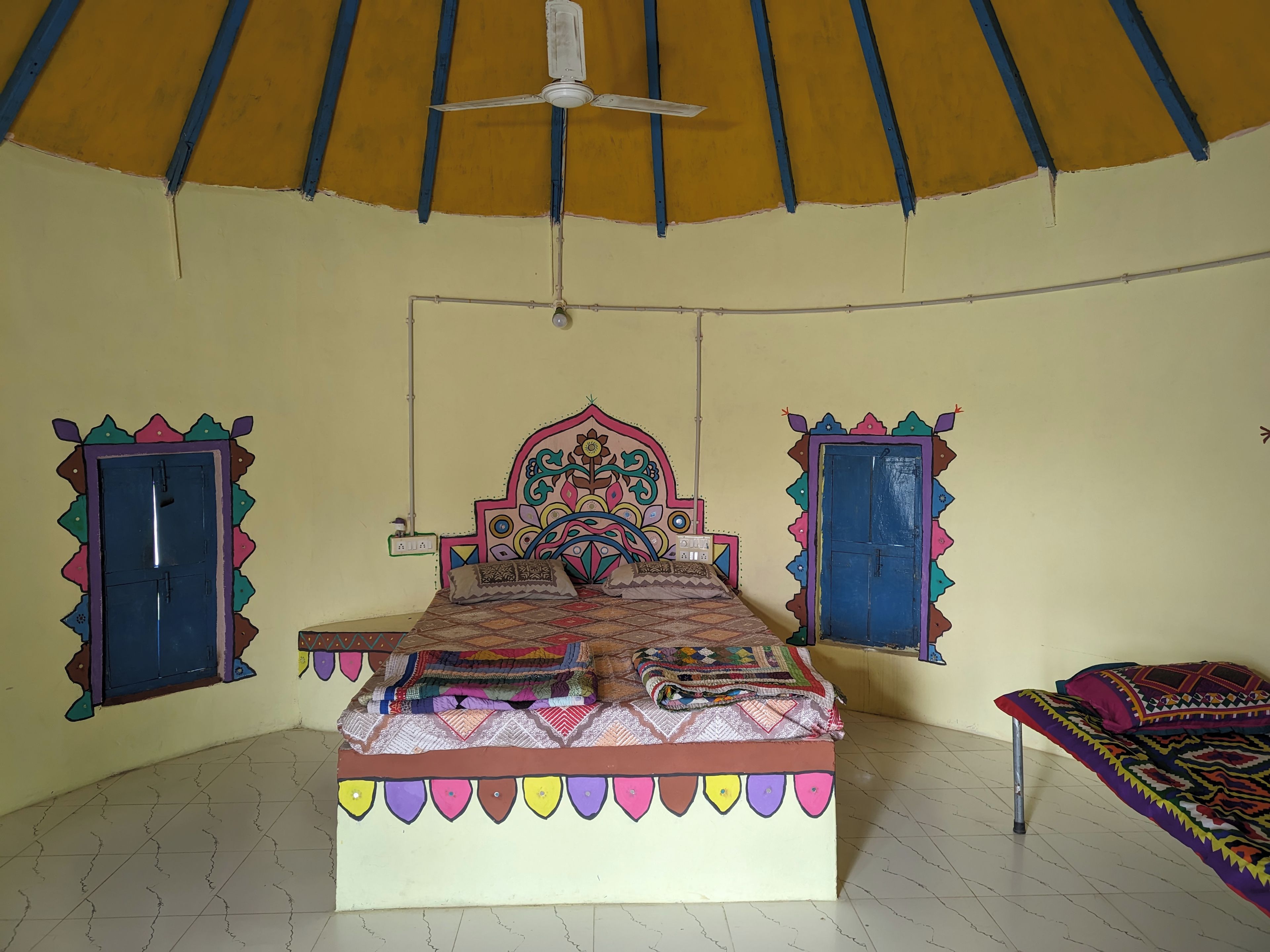Quarto com cama, ventoinha no teto e duas portas com molduras decorativas.