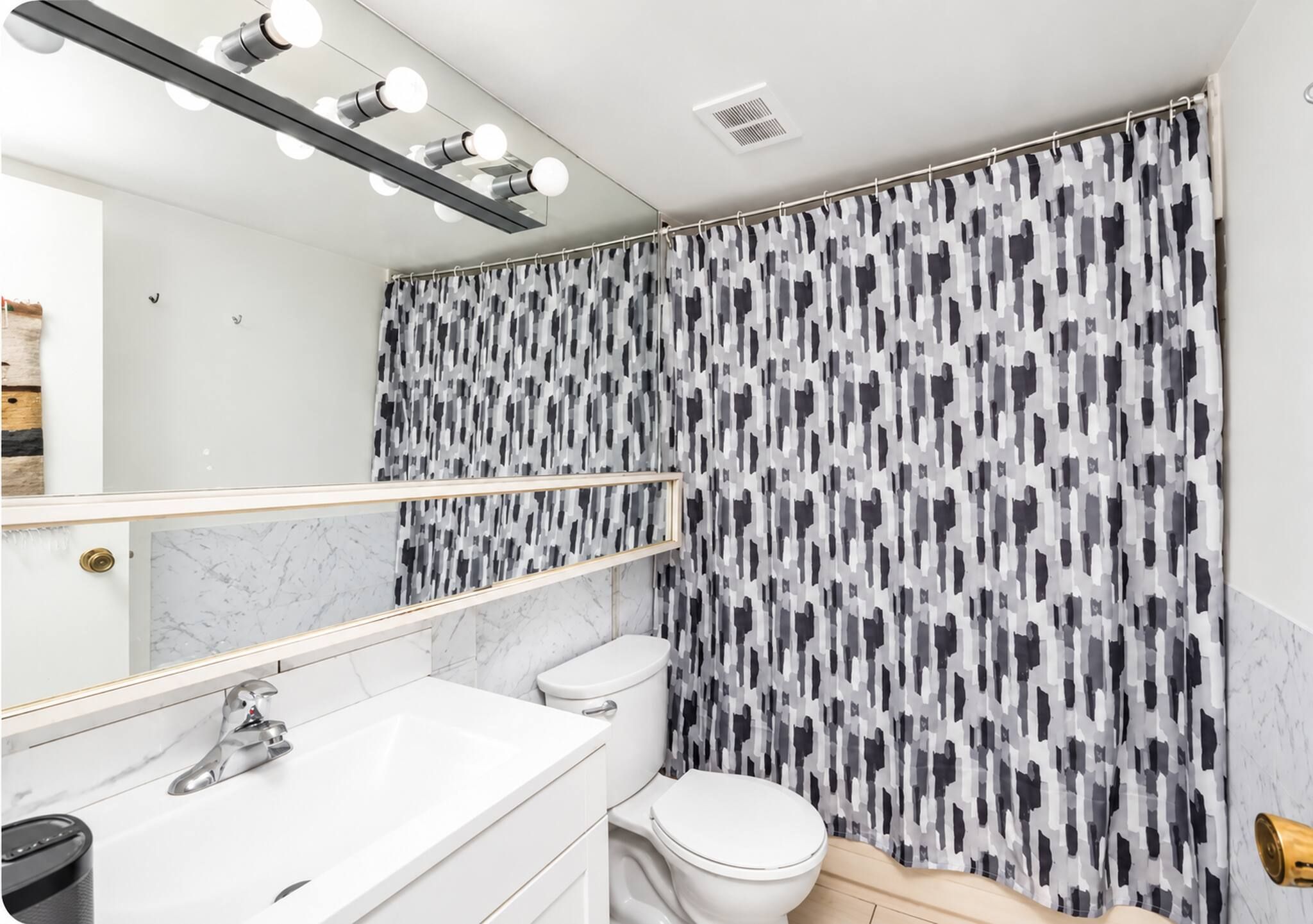 Casa de banho com toucador branco, sanita e separador de duche com padrão abstrato a preto e branco.