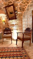 Um quarto com paredes de pedra, duas cadeiras de madeira com detalhes entalhados, um tapete estampado e um espelho grande na parede.