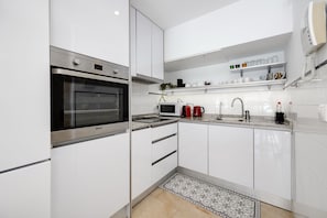 Cozinha moderna com forno embutido, micro-ondas e chaleira, armários brancos e painel de azulejos.