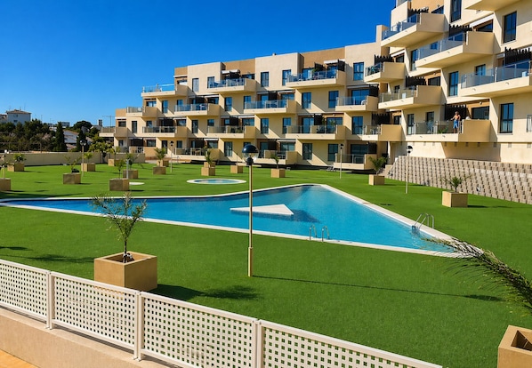 Um edifício moderno com apartamentos, piscina, gramados verdes e varandas.