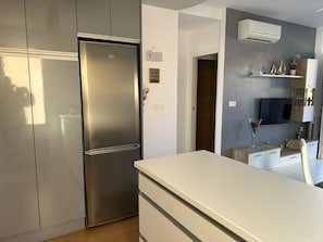 Cozinha moderna com geladeira de aço inoxidável, armários brancos e ar condicionado embutido.