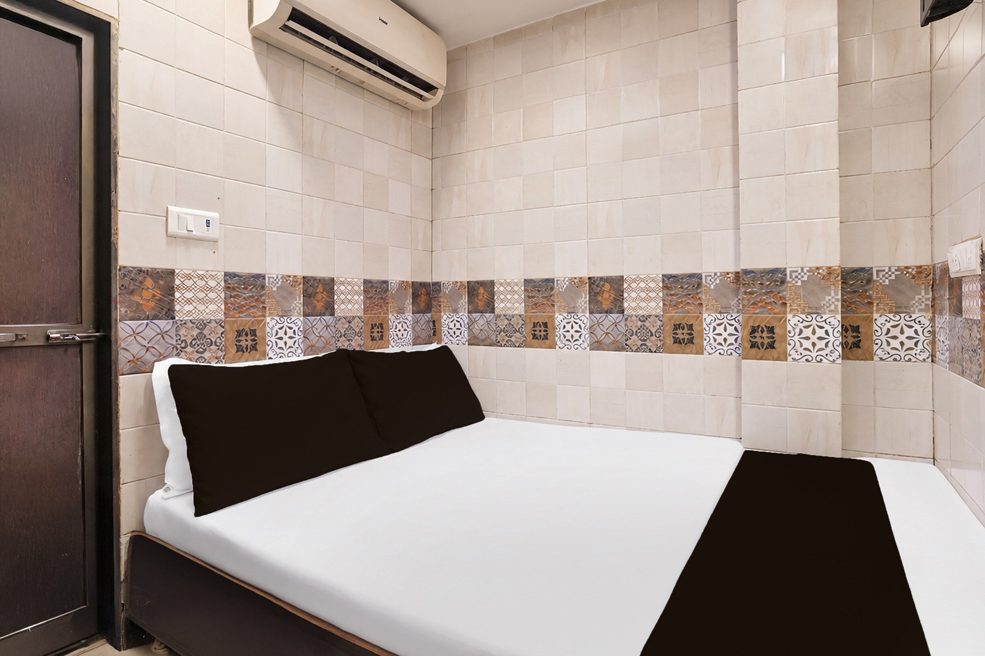 Quarto de hotel com cama, ar condicionado fixado na parede e rodapé de azulejos estampados.