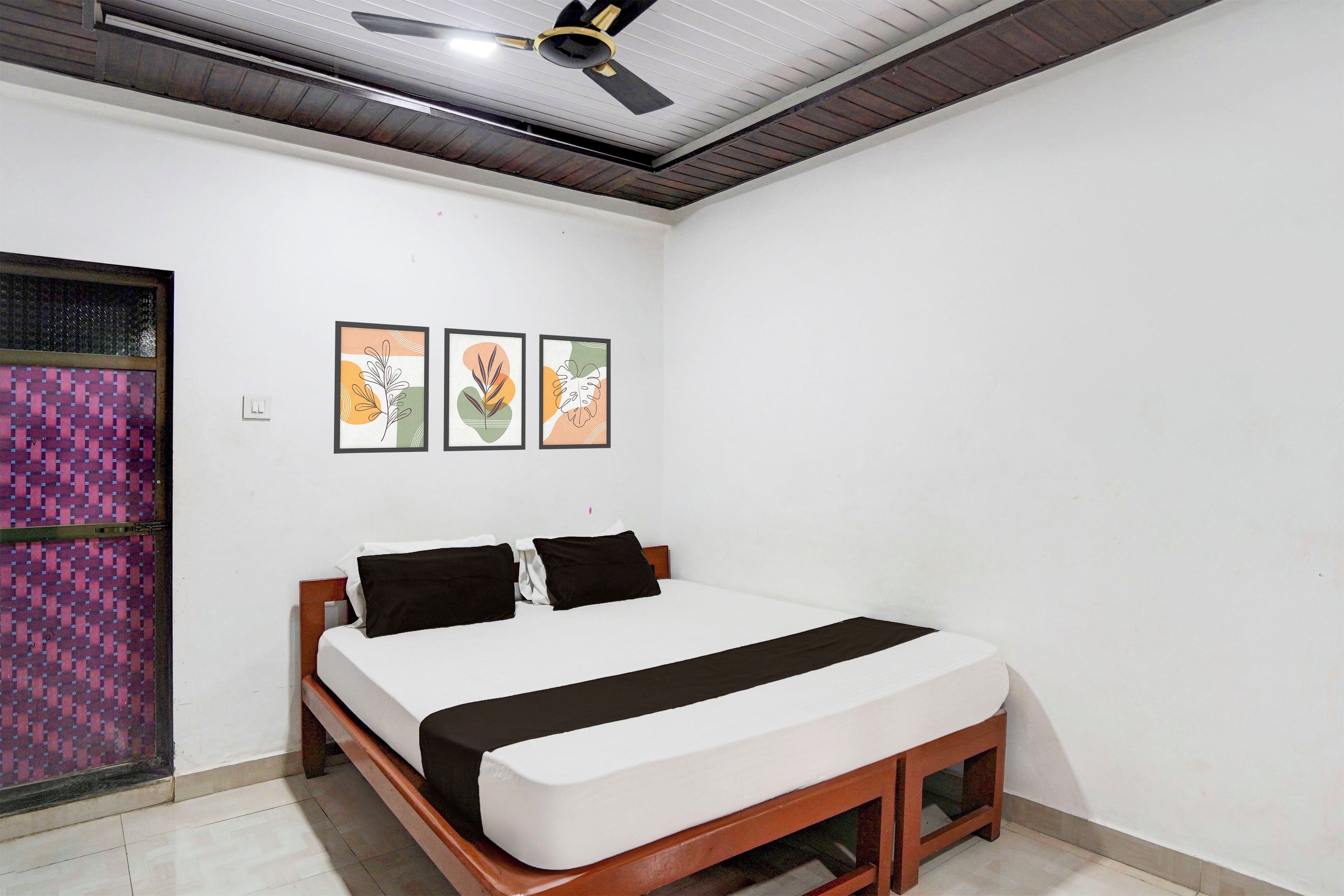 Quarto com cama, ventilador de teto e três obras de arte emolduradas na parede.