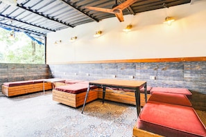 Interior de restaurante com teto alto, vigas aparentes e diversos tipos de assentos, incluindo bancos e uma mesa.
