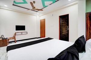 Quarto de hotel com cama, escrivaninha, cadeira, televisão e porta.