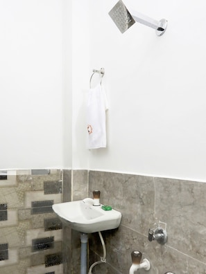 Casa de banho com lavatório branco, chuveiro manual e toalheiro com toalha branca.