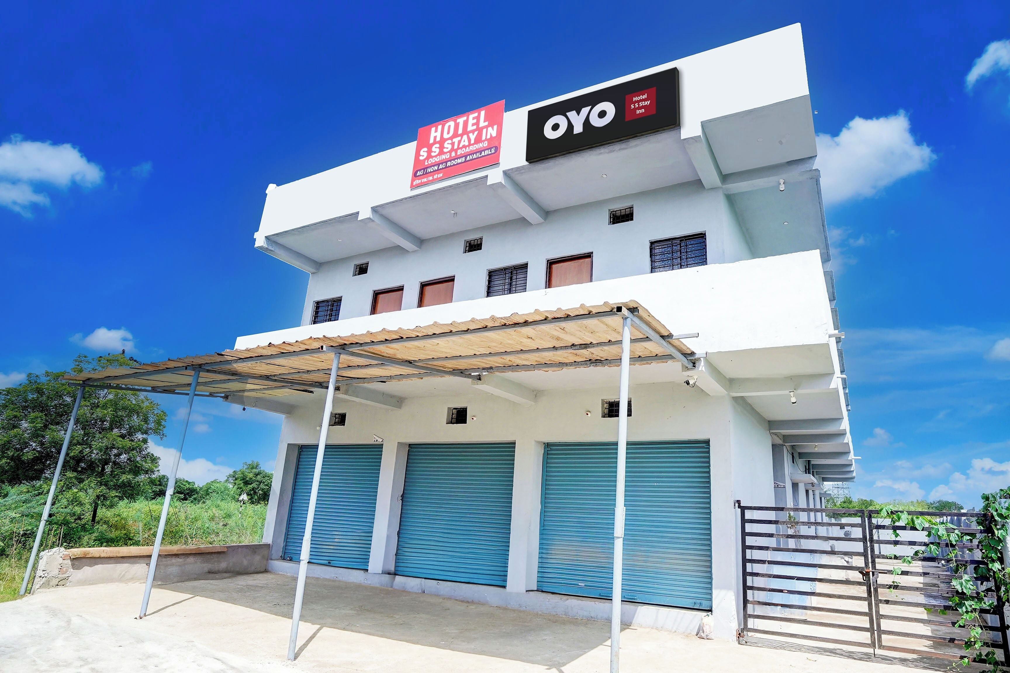Um hotel com uma placa indicando 'Hotel Stay In' e a marca 'OYO Inn', apresentando uma entrada coberta e várias portas de garagem fechadas.