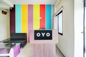 Uma área de recepção com parede colorida, sofá de couro preto, mesa de vidro e placa com a inscrição 'OYO'.