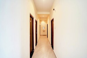 Corredor de hotel com portas de madeira, piso claro e uma pequena janela no final.