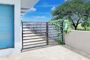 Uma entrada protegida por portão de metal, um toldo azul e um muro de concreto.