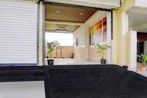 Entrada de edifício com persiana fechada, plantas em vasos e chão de azulejos.