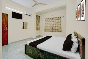 Quarto de hotel com cama, ventilador de teto, aparelho de ar condicionado, televisão de tela plana e janela com cortinas.