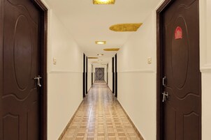 Corredor de hotel com portas de madeira, piso estampado e iluminação embutida.