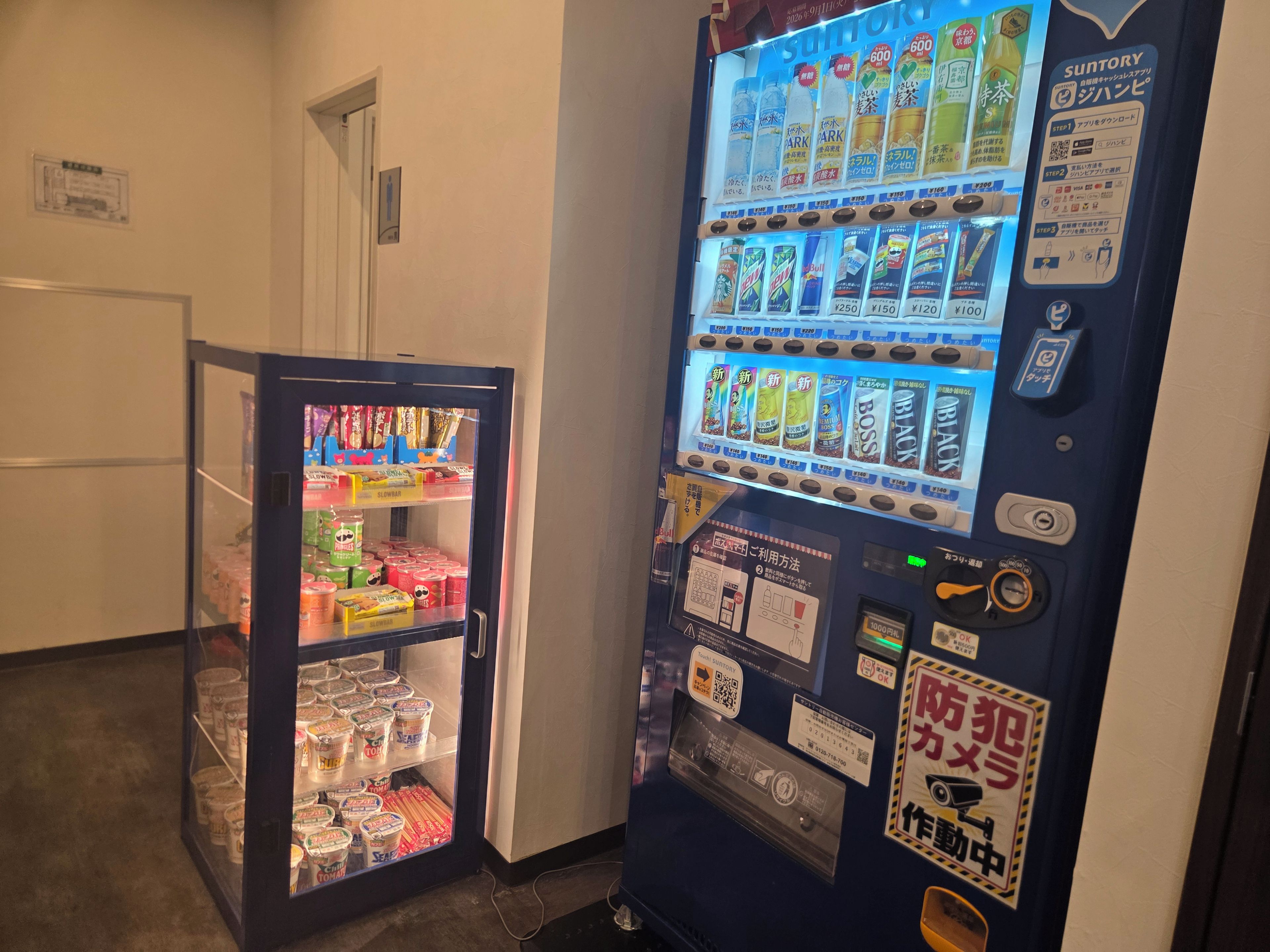 Máquina automática com diversas opções de bebidas e uma geladeira exposta com lanches e refrescos.