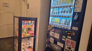 Máquina automática com diversas opções de bebidas e uma geladeira exposta com lanches e refrescos.