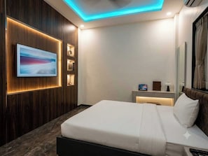 Quarto de hotel moderno com uma cama, televisão de tela plana na parede e mesa de cabeceira com abajur.