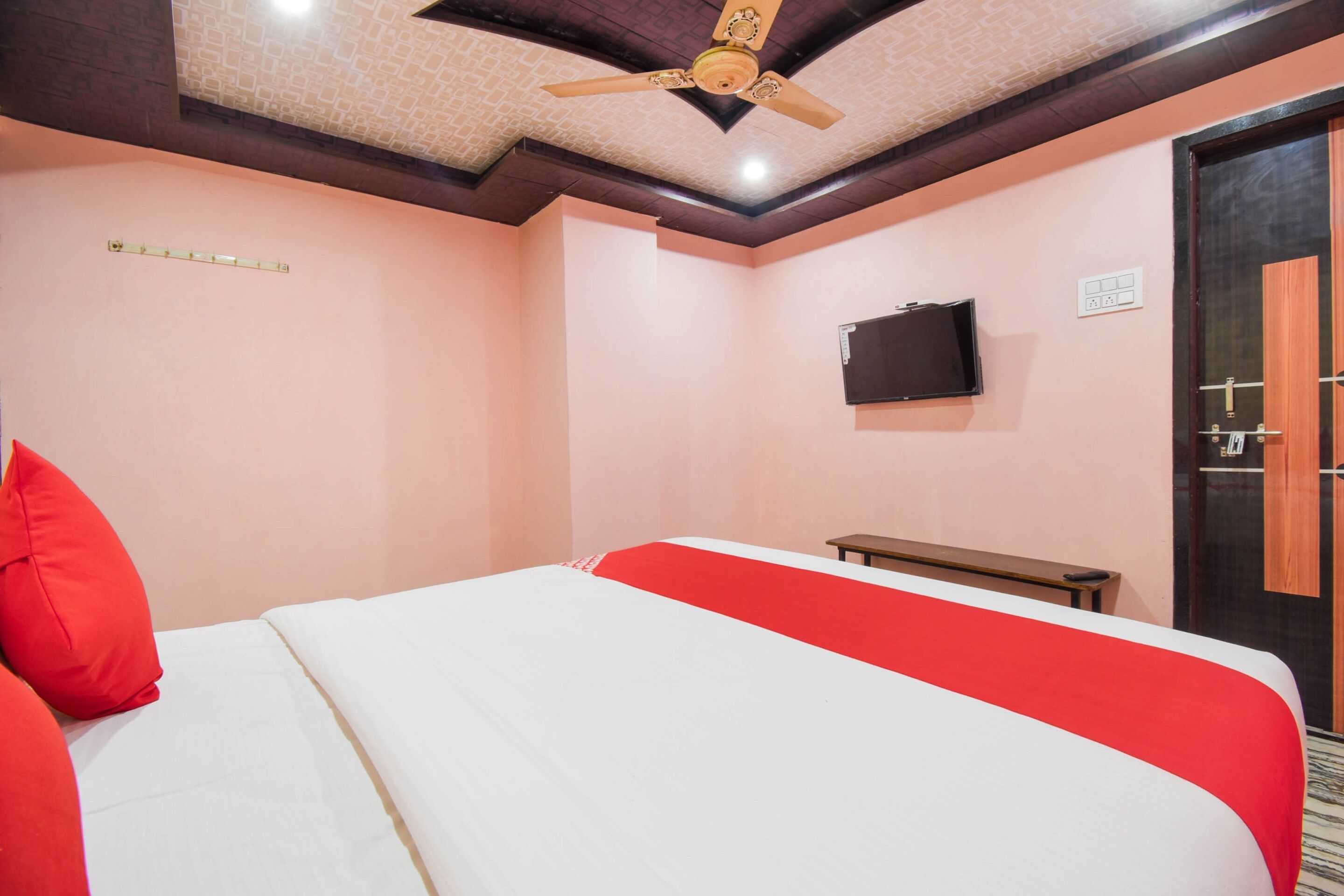 Quarto de hotel com cama, ventoinha no teto, televisão e porta.