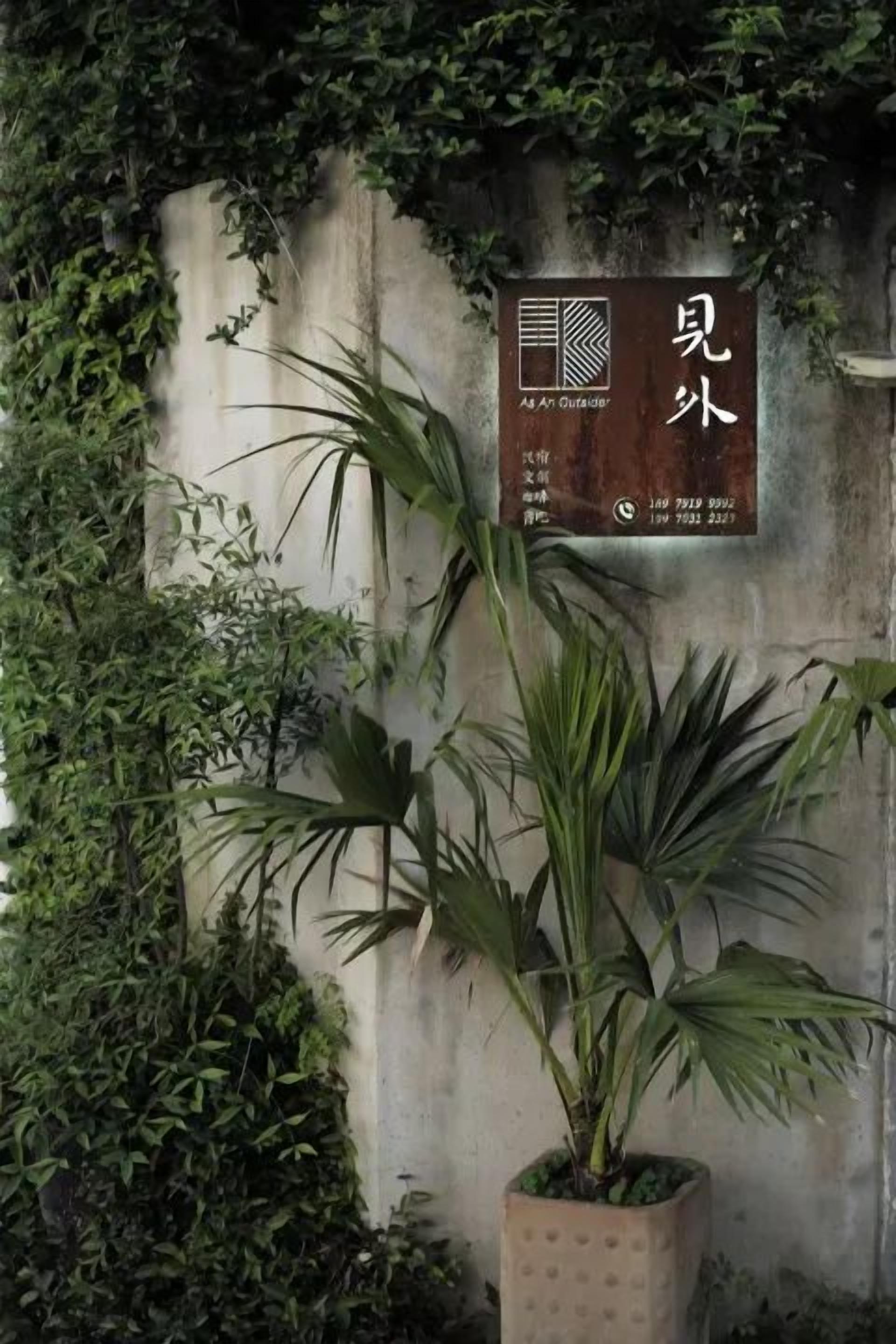 Placa com caracteres chineses, um vaso de planta e parede com plantas trepadoras.