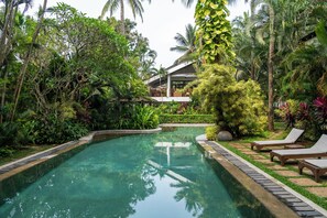 Piscina límpida rodeada por vegetação exuberante e um edifício com varanda.