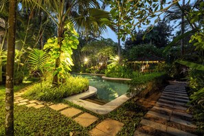 Um jardim com piscina, caminhos de pedra e vegetação exuberante.