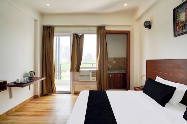 Quarto de hotel com cama, mesa de cabeceira com luminária, janela com cortinas e vista para prédios.