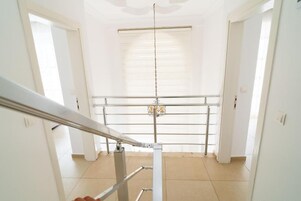 Corredor com corrimão de metal, um cesto de basquete e uma porta à direita.