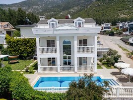 Uma casa de dois andares com varanda, piscina e vista para uma paisagem montanhosa.