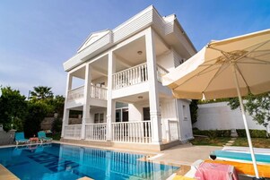 Um edifício de dois andares com piscina, área de estar ao ar livre e espaço coberto.