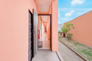 Um corredor com uma porta que dá para um quarto, uma pequena área de jardim e uma parede de tijolos.