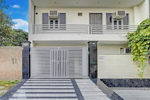 Um edifício de dois andares com portão fechado, aparelhos de ar condicionado e uma varanda.