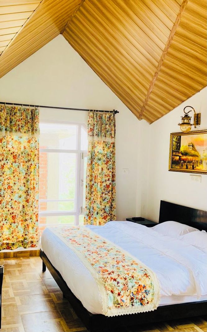 Quarto com cama, cortinas, mesa de cabeceira e luminária na parede.
