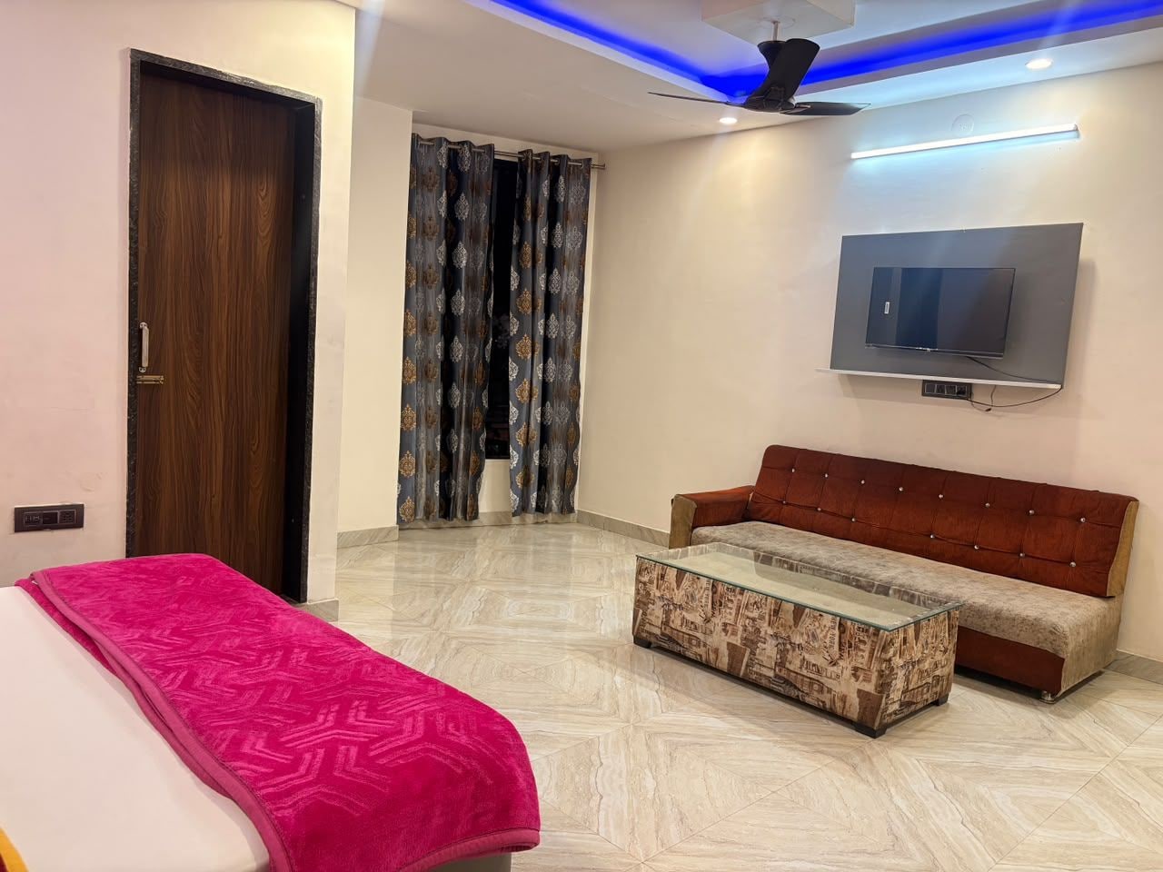 Quarto com cama, sofá, mesa de centro, televisão e ventoinha no teto.