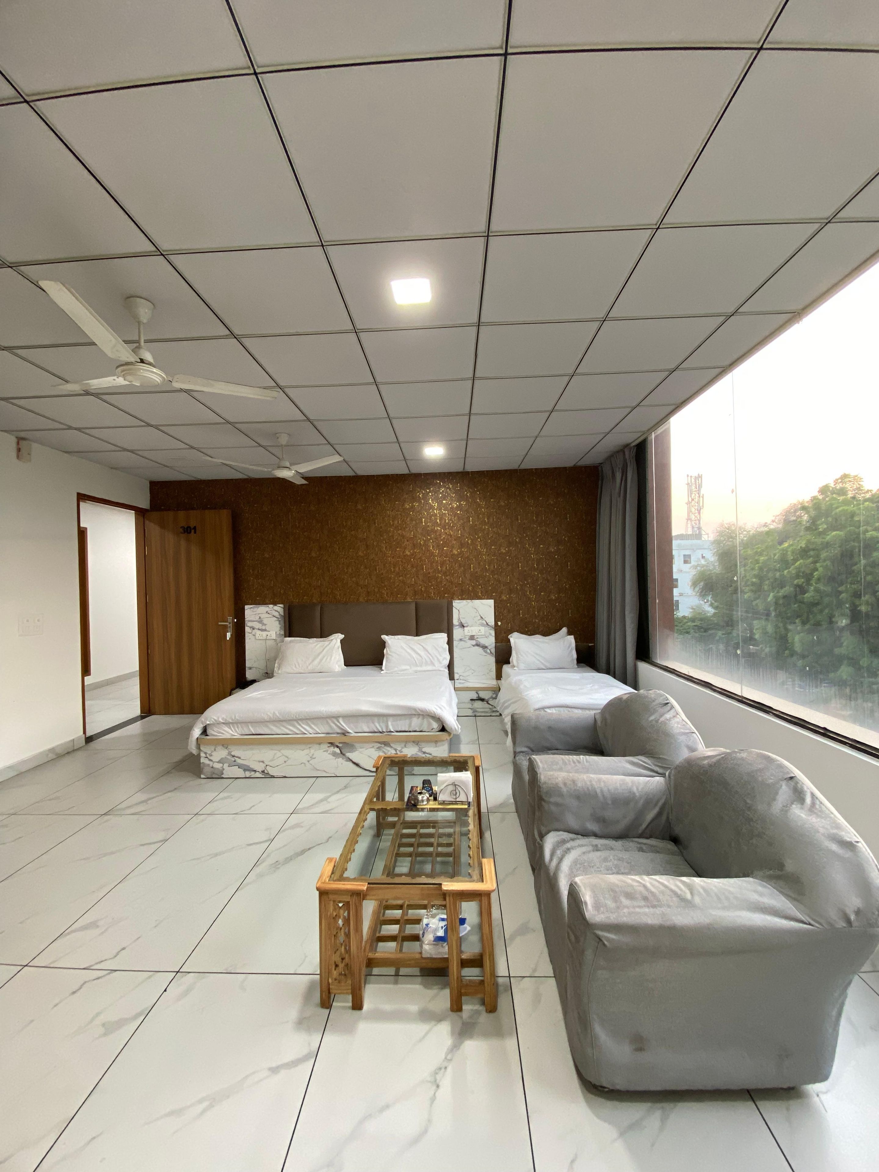 Quarto de hotel com cama grande, sofá, mesa de centro e vista para o exterior.